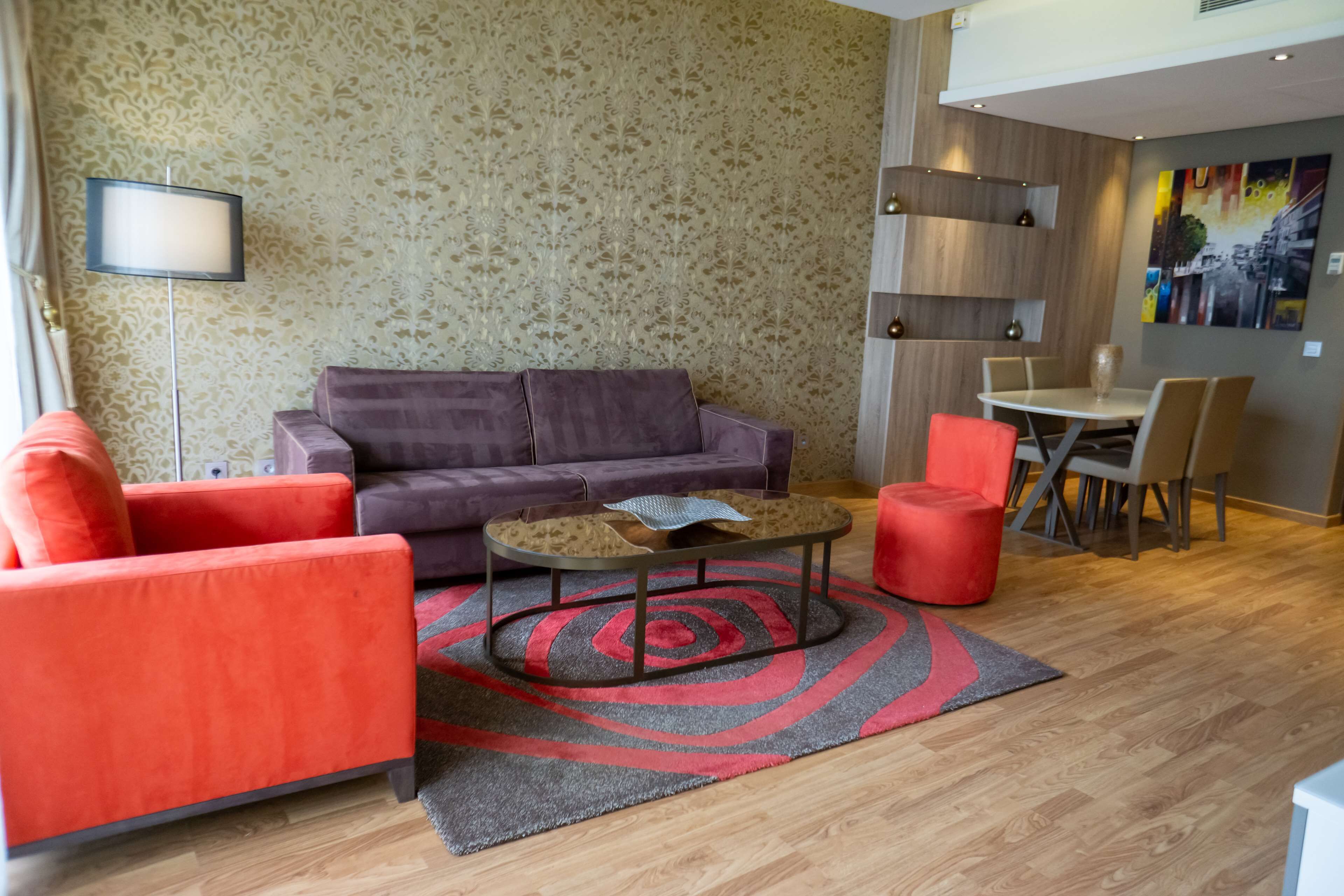 Uma sala de estar moderna com um sofá roxo, poltronas vermelhas, uma mesa de centro e um espaço de jantar com mesa e cadeiras.