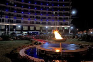 Hotel com uma grande fonte ao ar livre, área de estacionamento e um edifício com vários andares e luzes azuis.