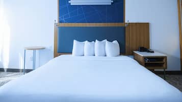 Quarto de hotel com uma cama grande, cabeceira de madeira, mesa de cabeceira com telefone e abajur, e uma pequena mesa redonda.
