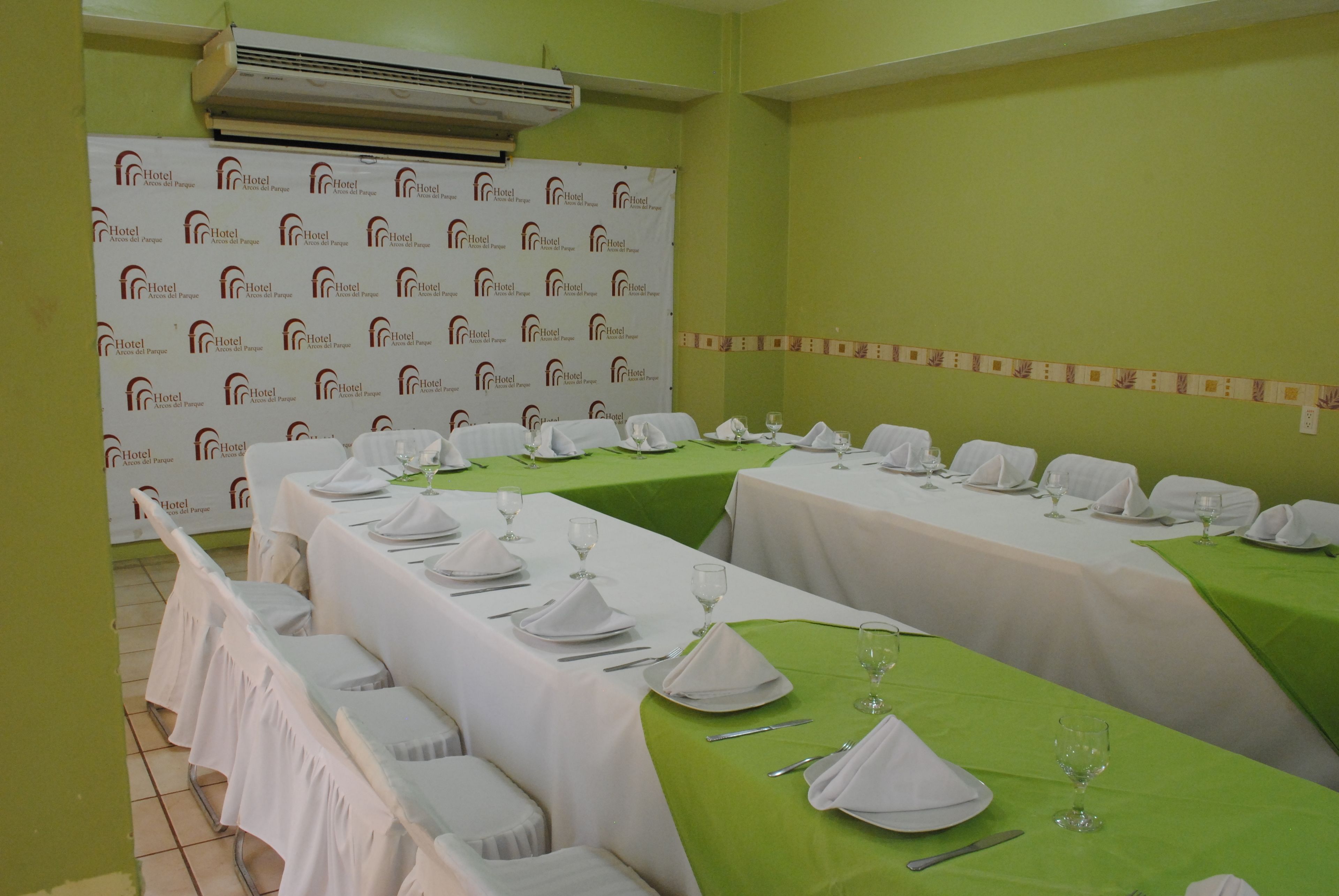 Sala de conferências com várias mesas preparadas para um evento formal, unidades de ar condicionado e um banner com o nome do hotel.