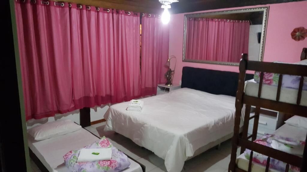 Quarto com uma cama de solteiro, uma cama menor, uma mesa de cabeceira, um espelho e cortinas cor-de-rosa.