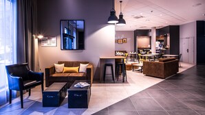 Uma sala de estar moderna com um sofá, poltronas e uma mesa de centro. Uma cozinha é visível ao fundo.