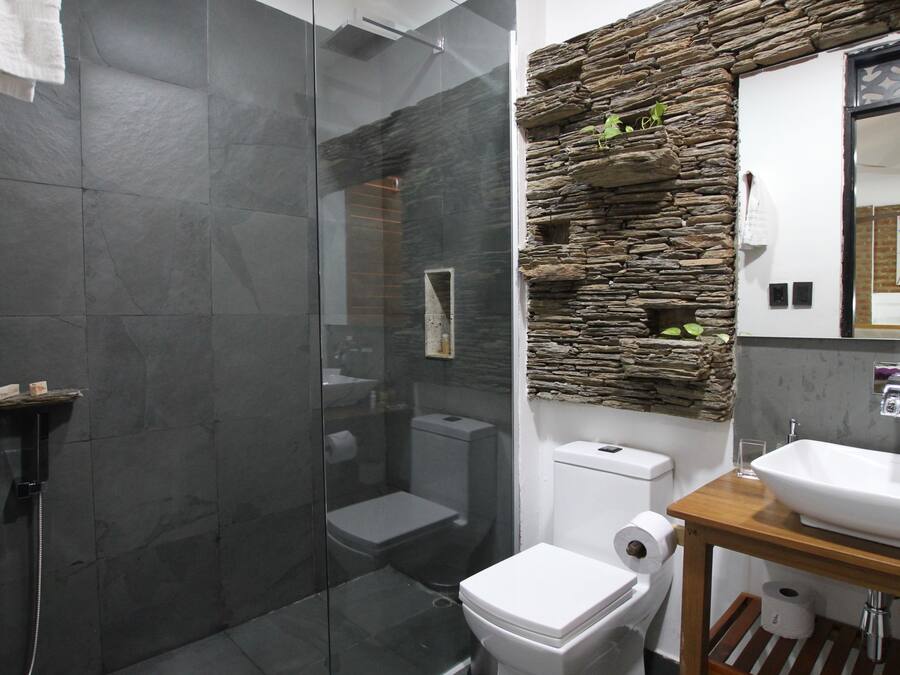 Uma casa de banho moderna com chuveiro em cabine de vidro, sanita branca e toucador de madeira com lavatório branco.