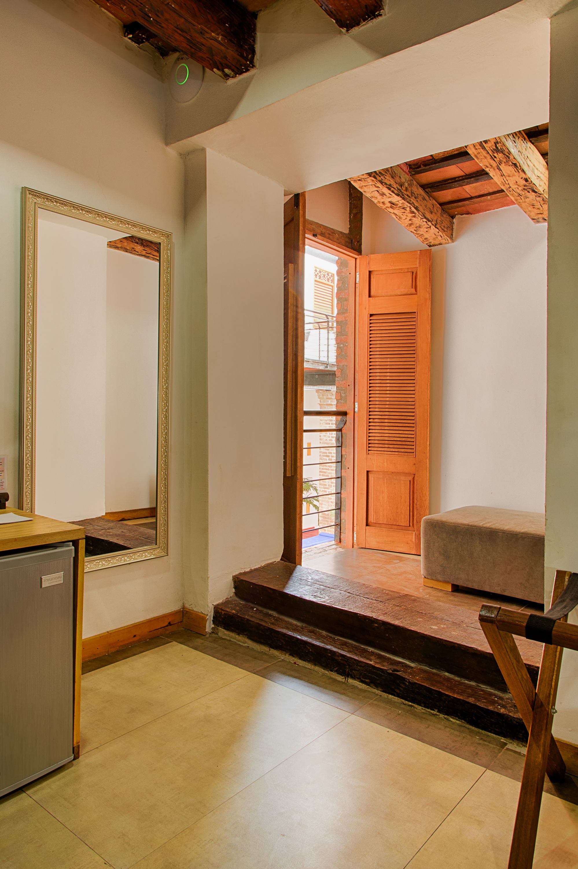 Um corredor com porta de madeira, um banco e um espelho.