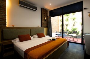 Quarto de hotel com uma cama grande, uma mesa de cabeceira, uma janela com vista para o exterior e uma pequena mesa com cadeiras.