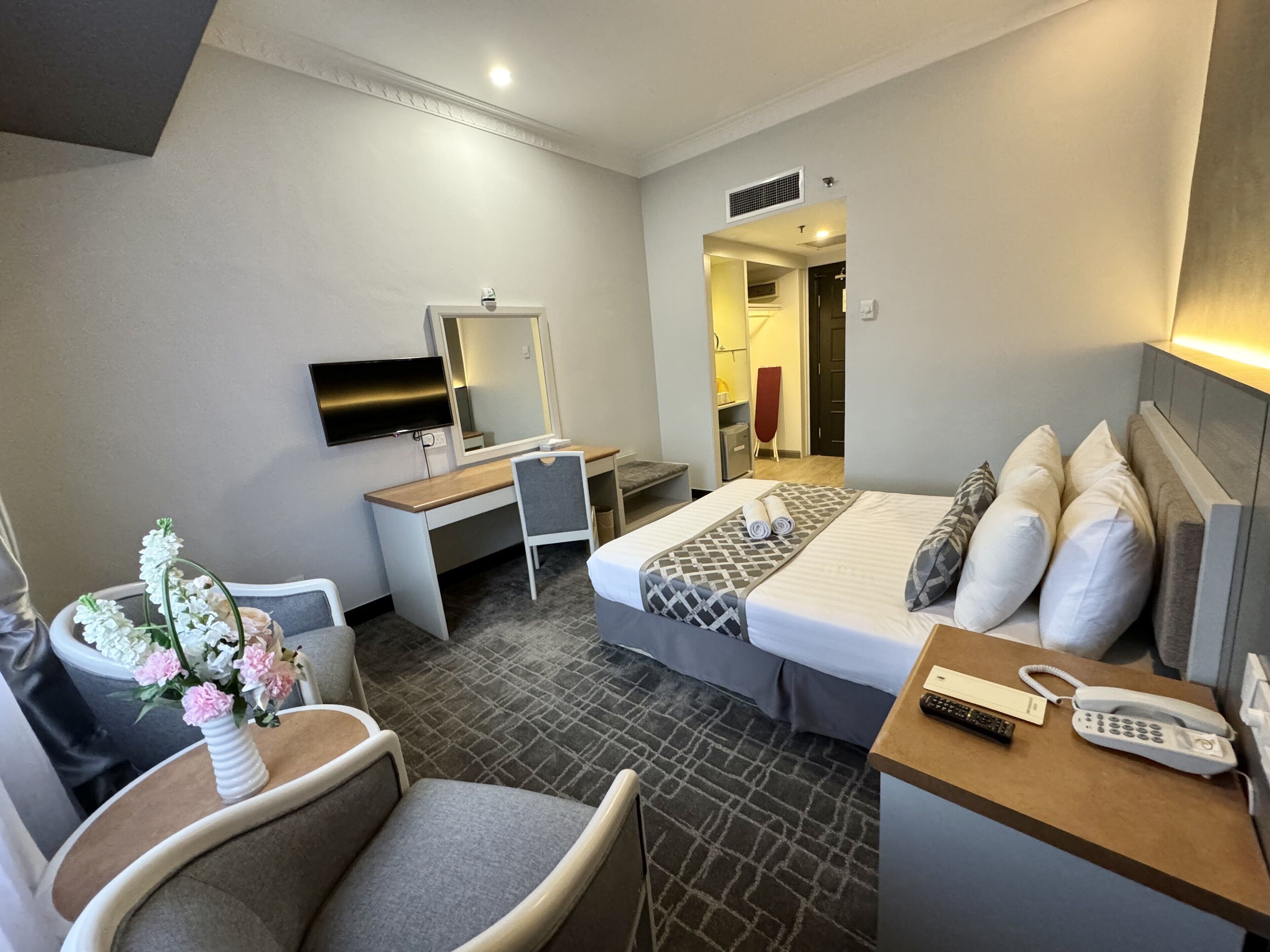 Quarto de hotel com cama, escrivaninha, cadeira e pequena mesa com telefone e controle remoto.
