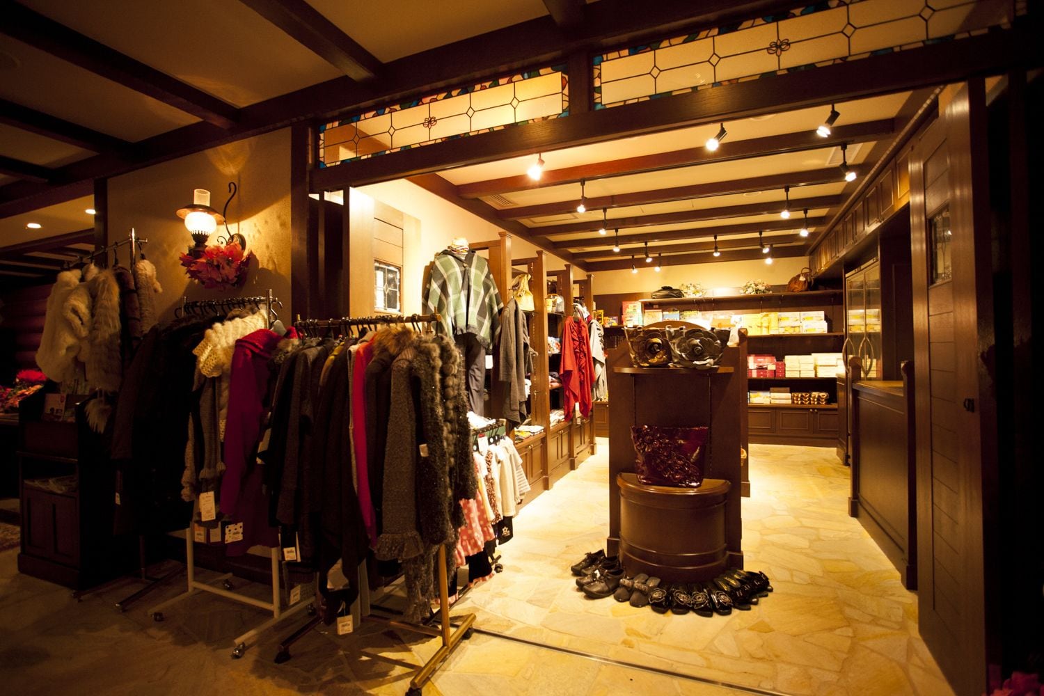 Uma loja de roupas boutique com araras de roupas de inverno, um display de sapatos e decoração em madeira.