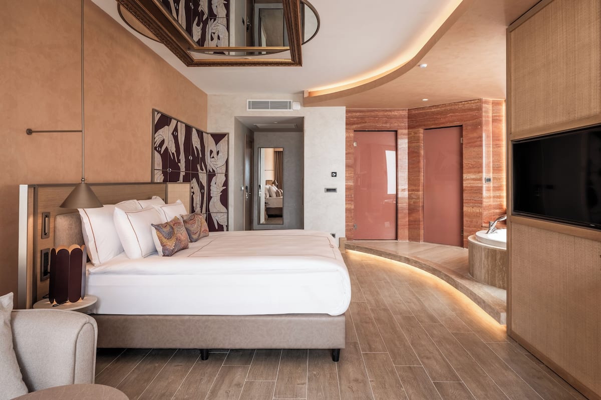 Quarto de hotel moderno com uma cama grande, televisão, banheiro com banheira e escada que leva a outro andar.