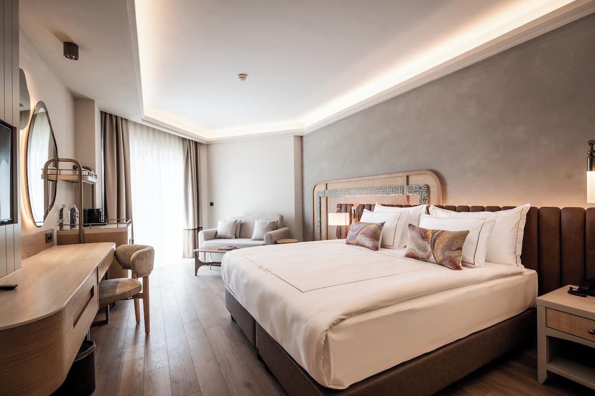 Quarto de hotel moderno com uma cama grande, uma escrivaninha, uma cadeira e uma televisão.