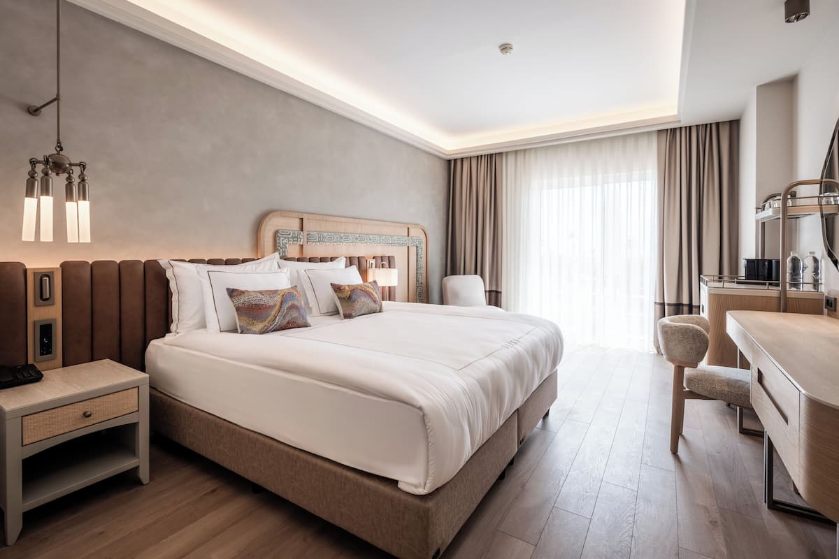 Quarto de hotel com cama grande, mesas de cabeceira, escrivaninha e espelho.