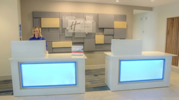 Bancada de recepção com a placa Holiday Inn Express, um folheto de boas-vindas e design moderno e minimalista.