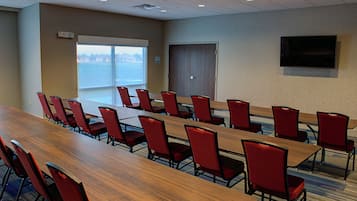 Uma sala de conferências com uma mesa comprida e cadeiras vermelhas, uma porta e uma TV na parede.