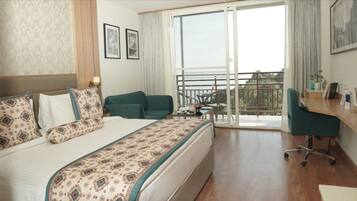 Quarto de hotel com cama, escrivaninha, cadeira e varanda com vista.