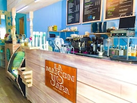 Interior de café com balcão de madeira, quadros de menu e equipamentos para preparo de café.
