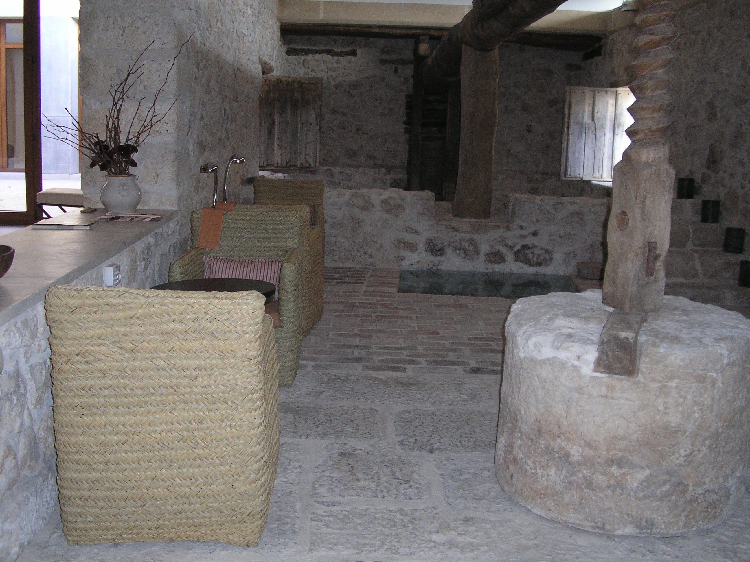 Interior com paredes de pedra, móveis de vime trançado, um pilar de pedra e uma janela com persianas de madeira.
