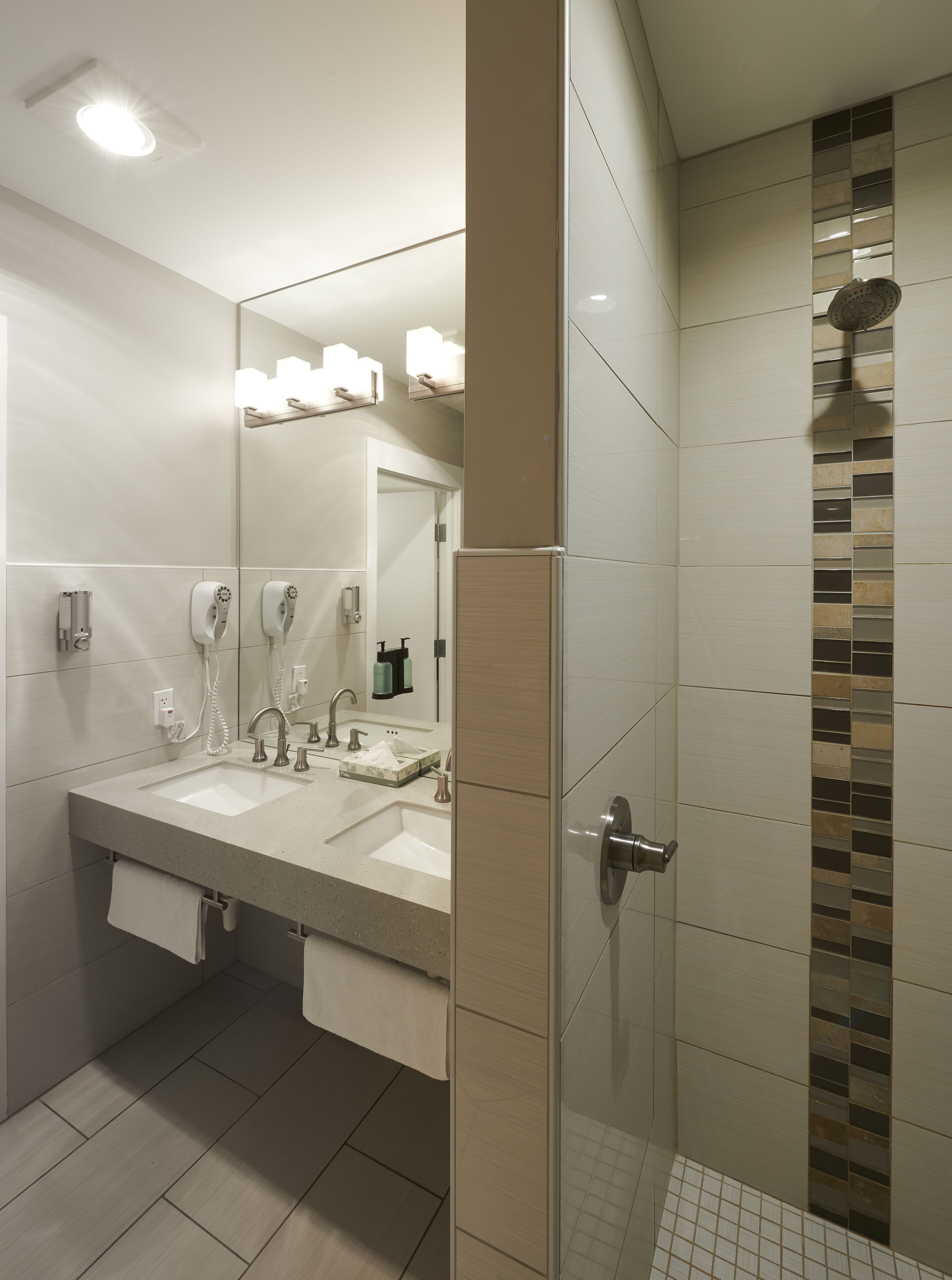 Uma casa de banho moderna com duas lavatórios, um espelho e zona de duche.