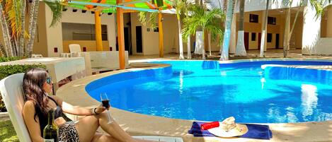 Uma área à beira da piscina com uma espreguiçadeira, uma garrafa de vinho e um smartphone sobre uma mesinha.