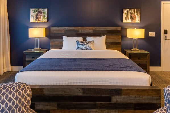 Cama bem arrumada com cabeceira de madeira, duas mesas de cabeceira com abajures e duas obras de arte na parede.