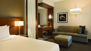 Quarto de hotel com uma cama grande, uma escrivaninha, um sofá e um pequeno banquinho.