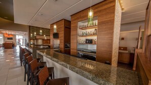Uma área de bar moderna com bancada de granito, detalhes em madeira e luminárias pendentes.
