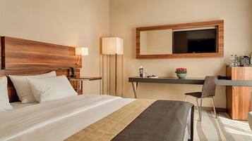 Quarto de hotel com cama, escrivaninha, cadeira, televisão e luminária.