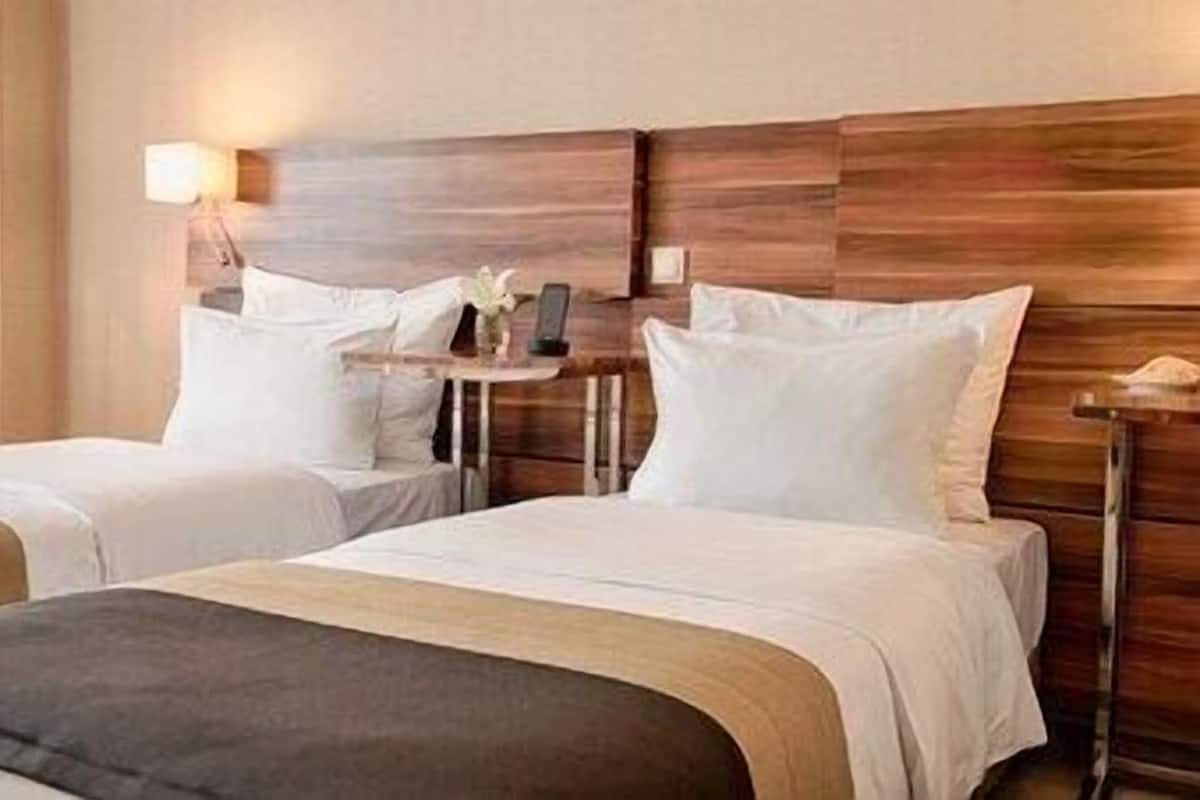 Quarto de hotel com duas camas, cabeceiras de madeira, mesas de cabeceira e uma luminária.