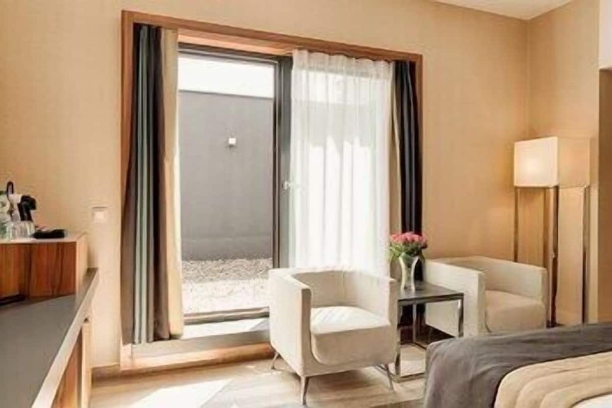 Quarto de hotel com cama, escrivaninha, cadeira, mesa pequena com um vaso e vista para o exterior.