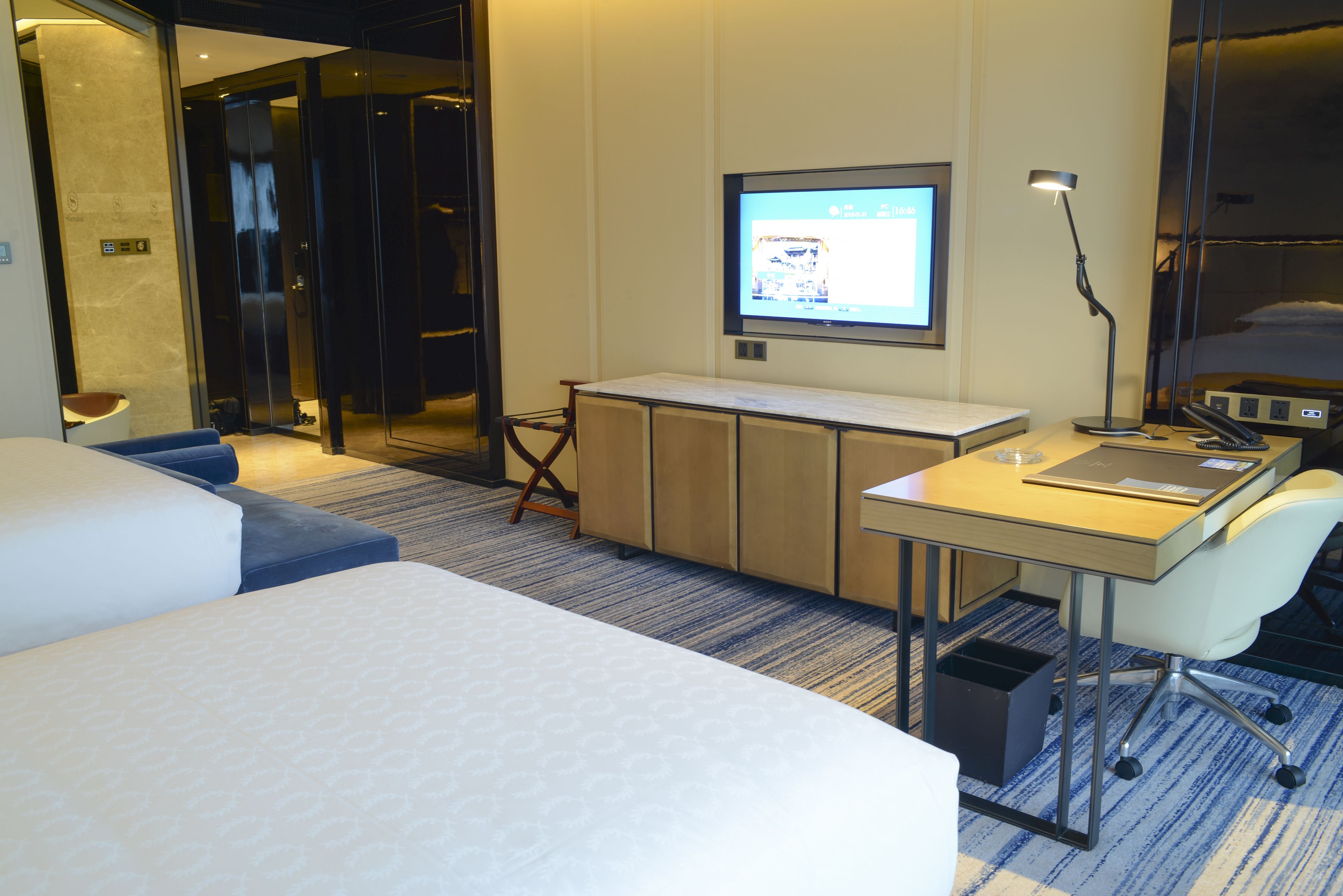 Quarto de hotel com cama, escrivaninha, cadeira, televisão e banheiro.