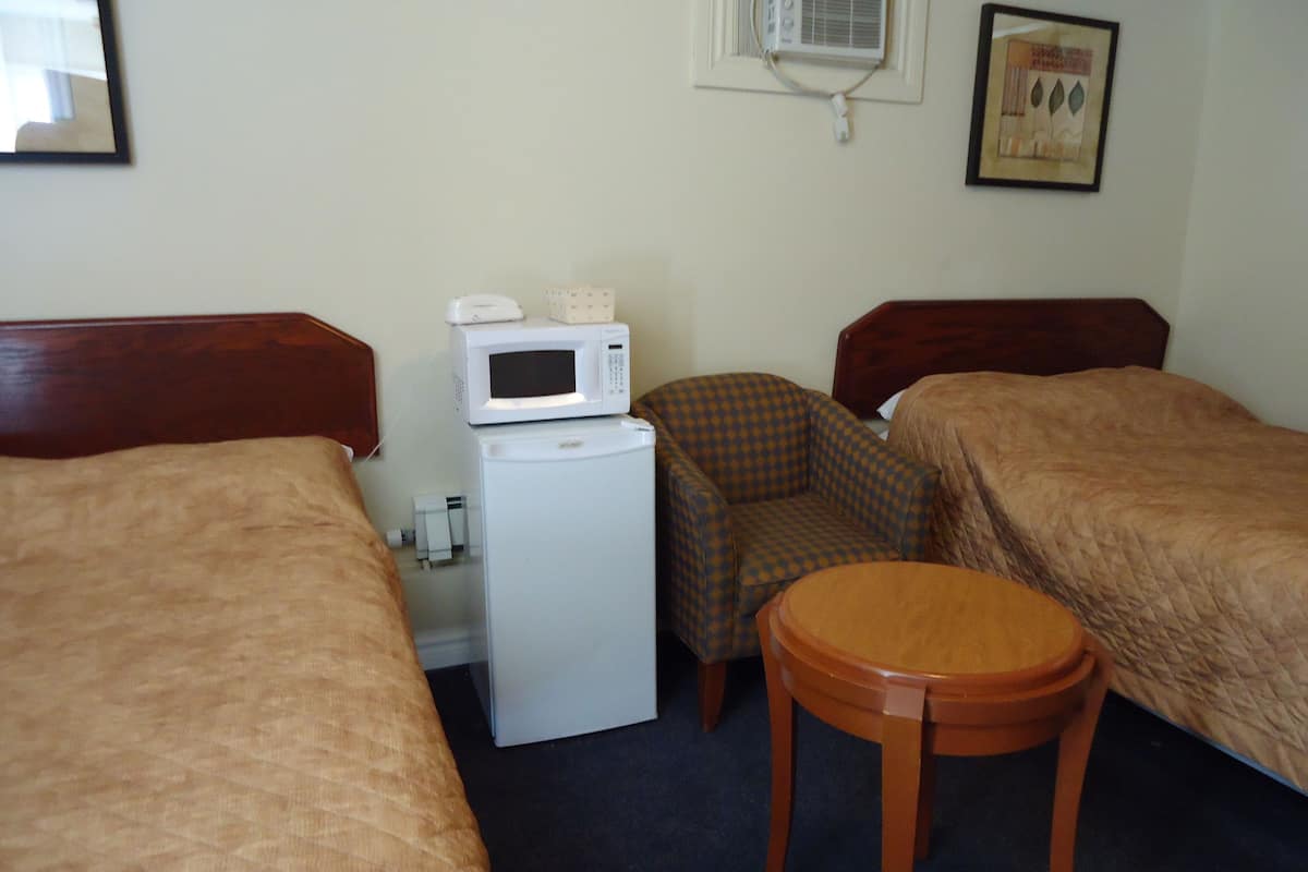 Quarto de hotel com duas camas de solteiro, uma mesa pequena, micro-ondas e frigorífico.