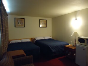 Quarto de hotel com duas camas, uma mesa pequena, uma luminária e um refrigerador.