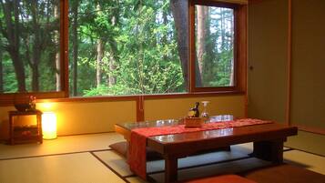Um quarto japonês tradicional com tatames, uma mesa de madeira baixa e vista para uma floresta através de amplas janelas.