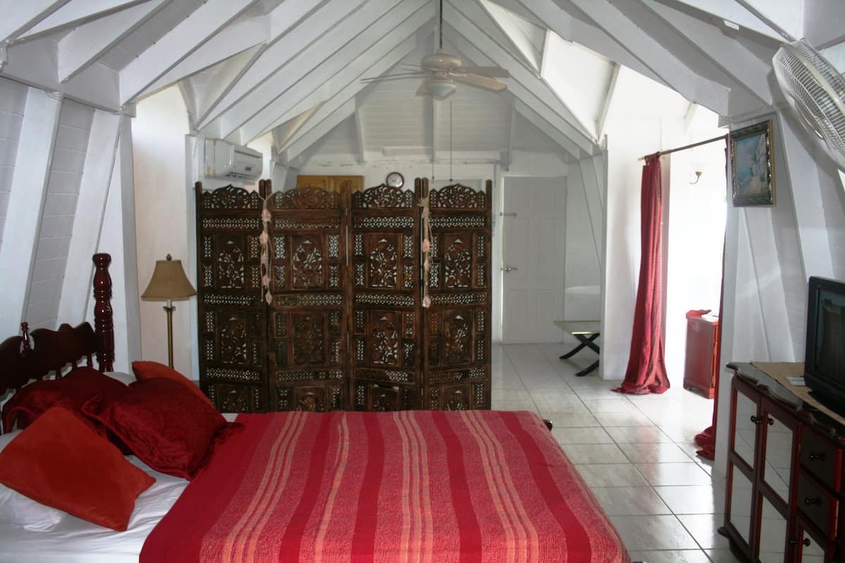 Quarto com cama, guarda-roupa de madeira, ventoinha no teto e televisão.