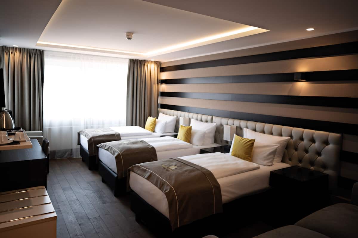 Quarto de hotel com duas camas, uma mesa de trabalho e uma janela grande com cortinas.