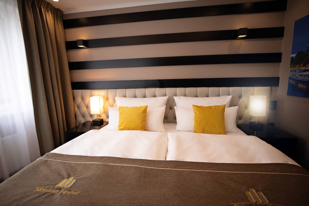 Quarto de hotel com uma cama grande, duas mesas de cabeceira com luminárias, uma parede listrada e uma cortina.