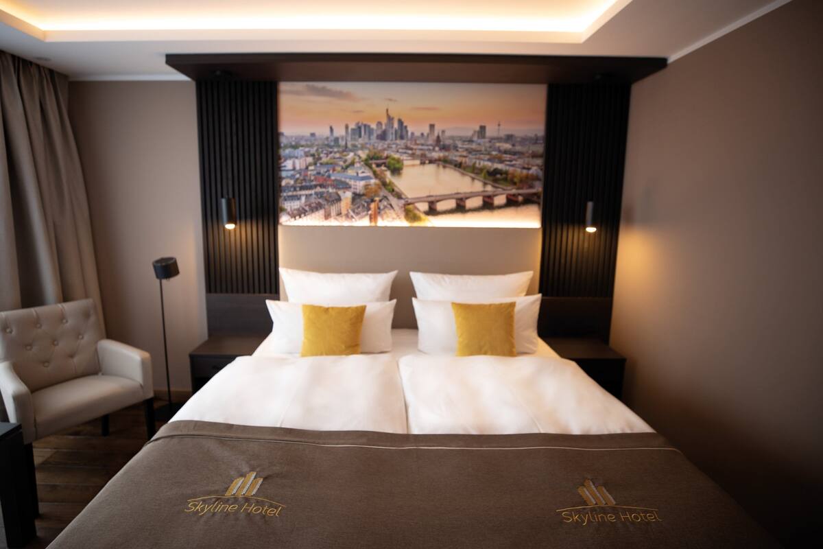 Quarto de hotel com uma cama grande, vista para a cidade, um sofá e um abajur.