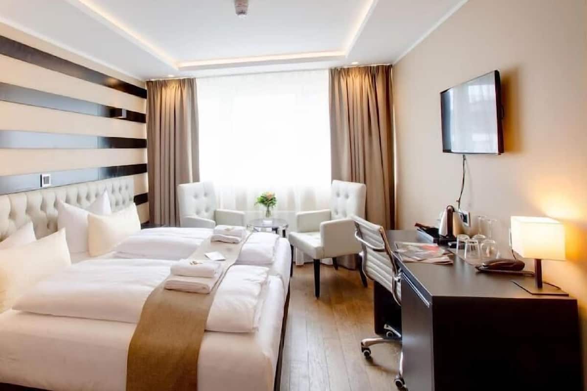 Quarto de hotel com uma cama grande, uma escrivaninha, uma cadeira e uma televisão.
