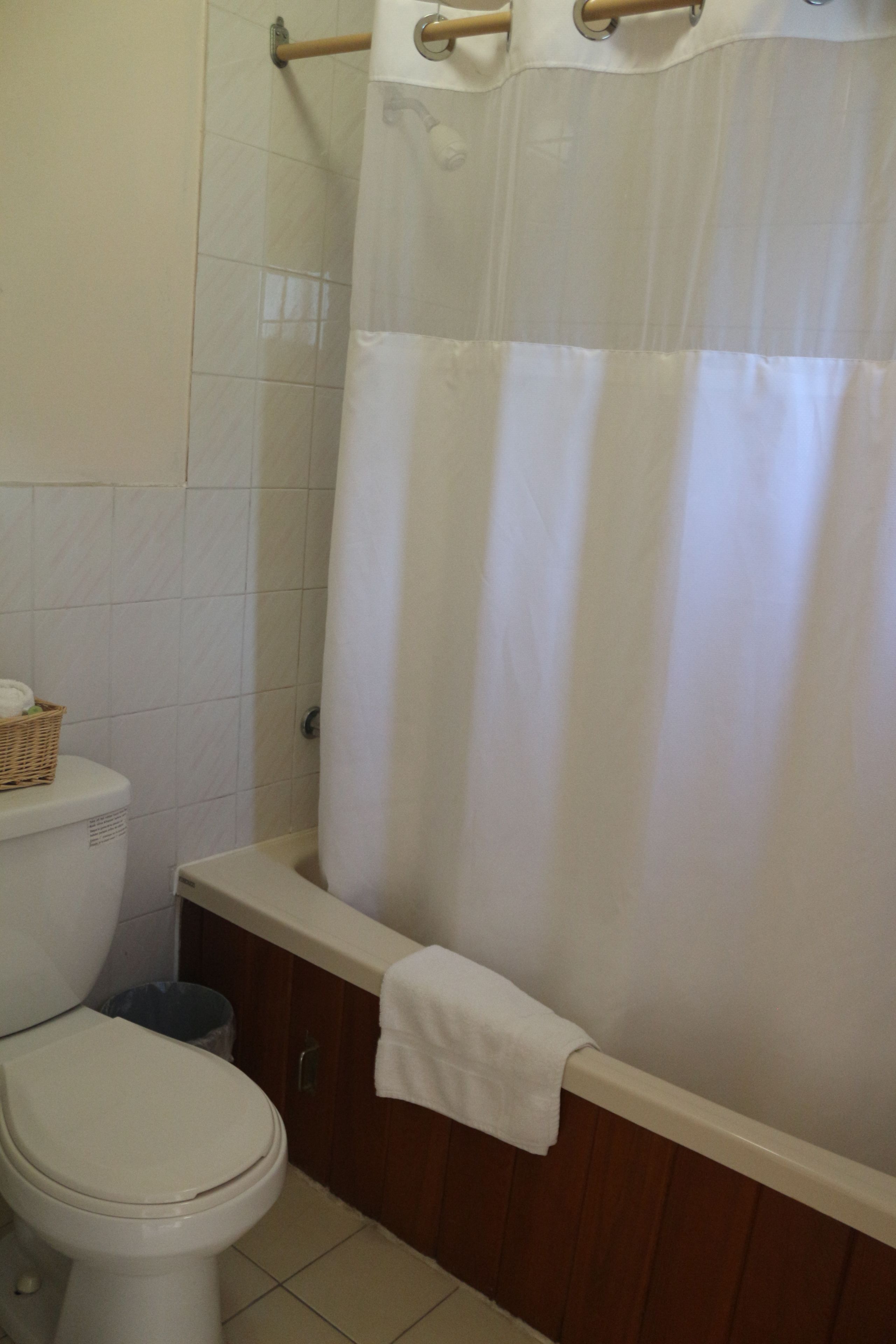 Casa de banho com sanita, armário de madeira e banheira com cortina de chuveiro branca.