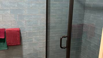 Um chuveiro com paredes de vidro, parede revestida com azulejos e porta-toalhas com toalhas vermelhas e verdes.
