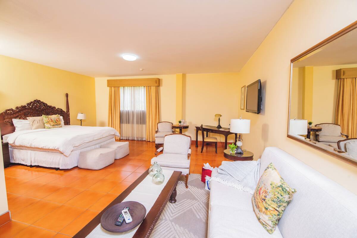 Quarto de hotel com cama de casal, sofá, mesa de jantar e televisão.