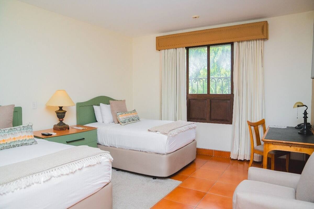Quarto de hotel com duas camas, uma escrivaninha e uma cadeira.