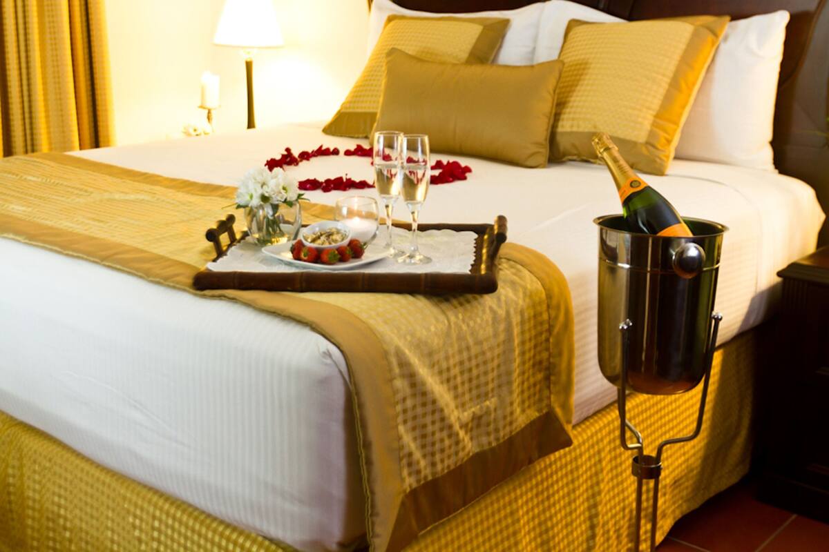 Quarto de hotel com cama bem arrumada, bandeja com comida e bebidas, e uma garrafa de champanhe em balde.