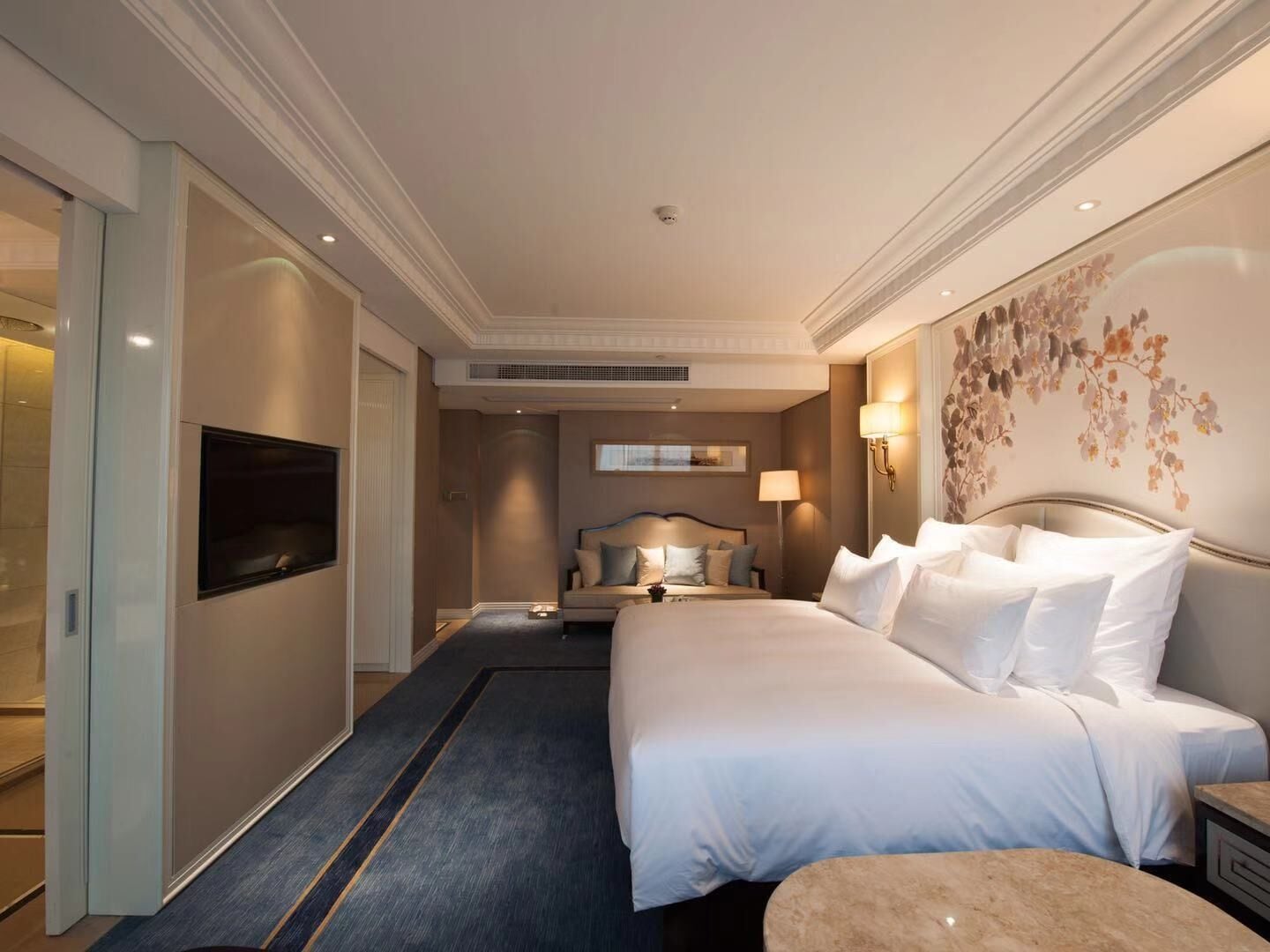 Quarto de hotel com cama grande, televisão, sofá e decoração na parede.