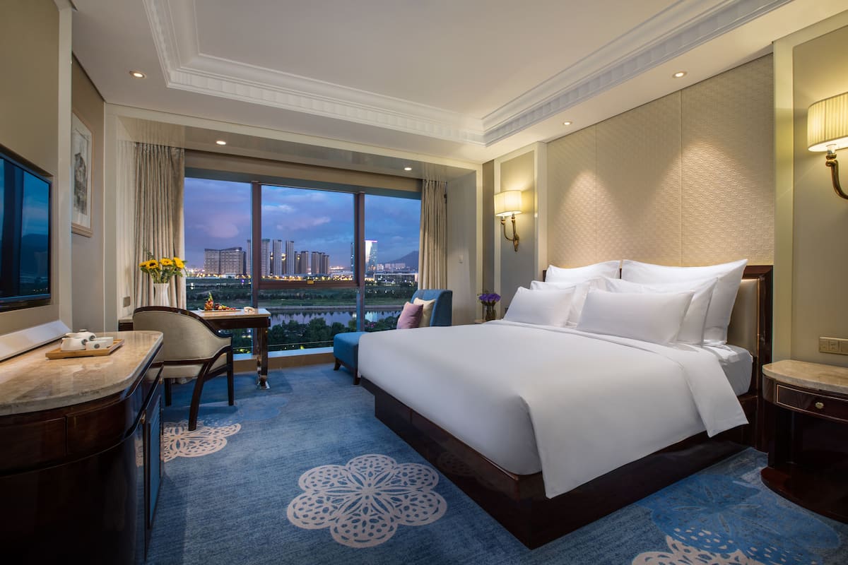 Quarto de hotel com uma cama grande, uma mesa, uma cadeira e vista para a cidade.