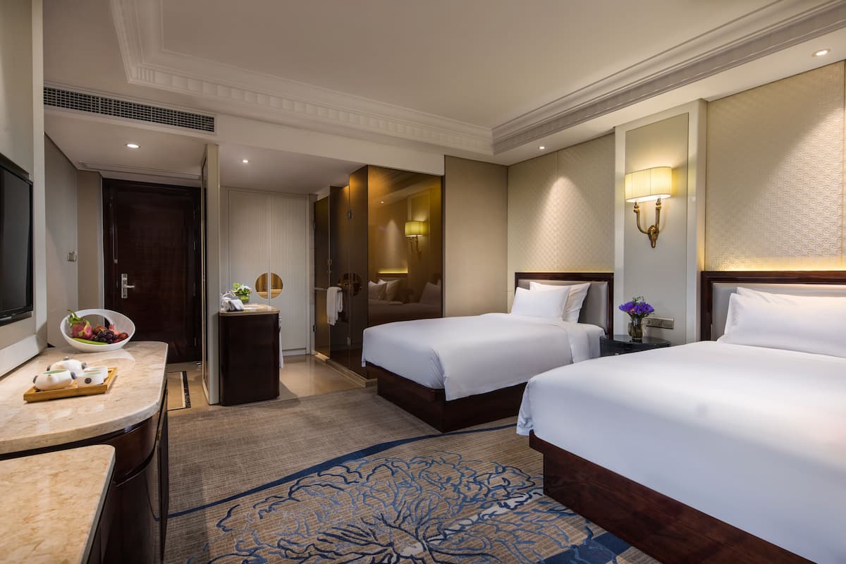 Quarto de hotel com duas camas, uma secretária, uma casa de banho e uma janela grande.
