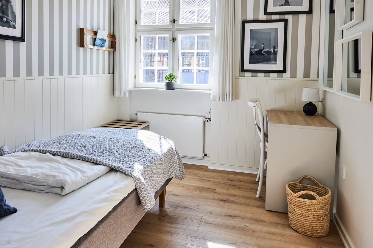Quarto bem arrumado com uma cama, uma escrivaninha e janela com vista para edifícios.