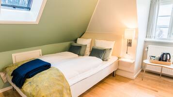 Quarto com cama, mesa de cabeceira, abajur, radiador e janela.