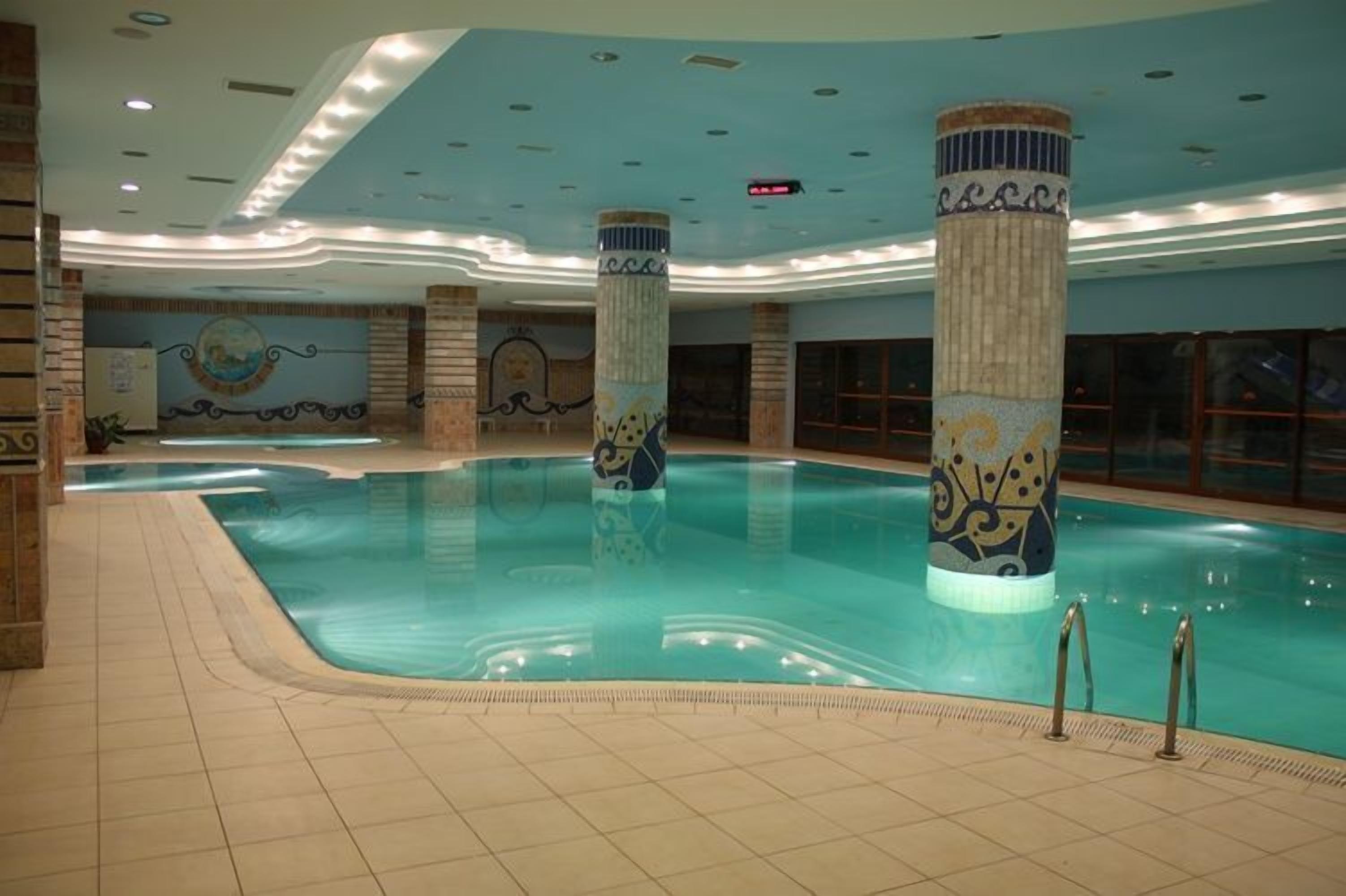 Piscina interna com pilares decorativos, piso revestido e teto com iluminação embutida.