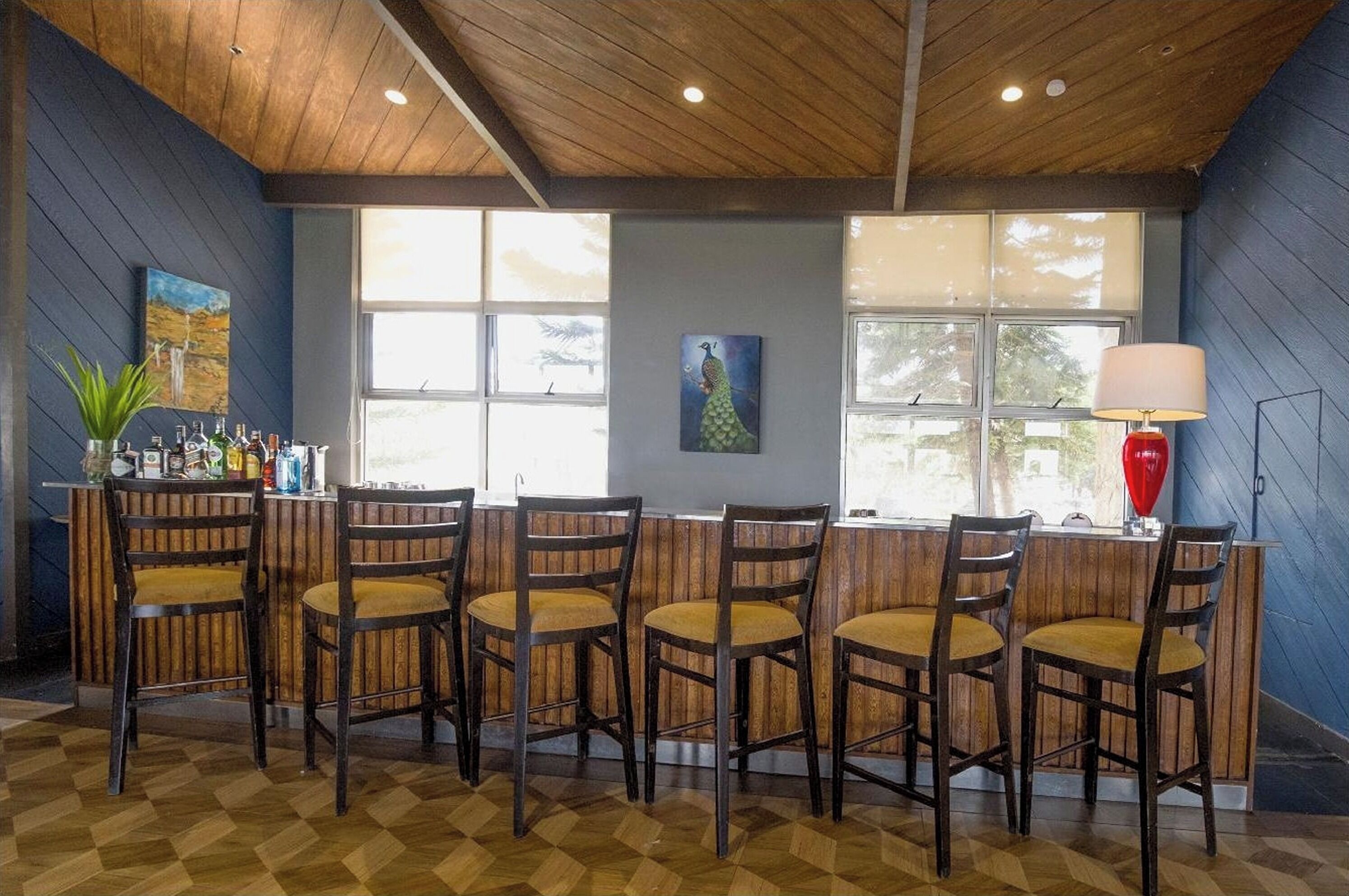 Uma área de refeições com cadeiras e mesas de madeira, um bar com garrafas e obras de arte nas paredes.