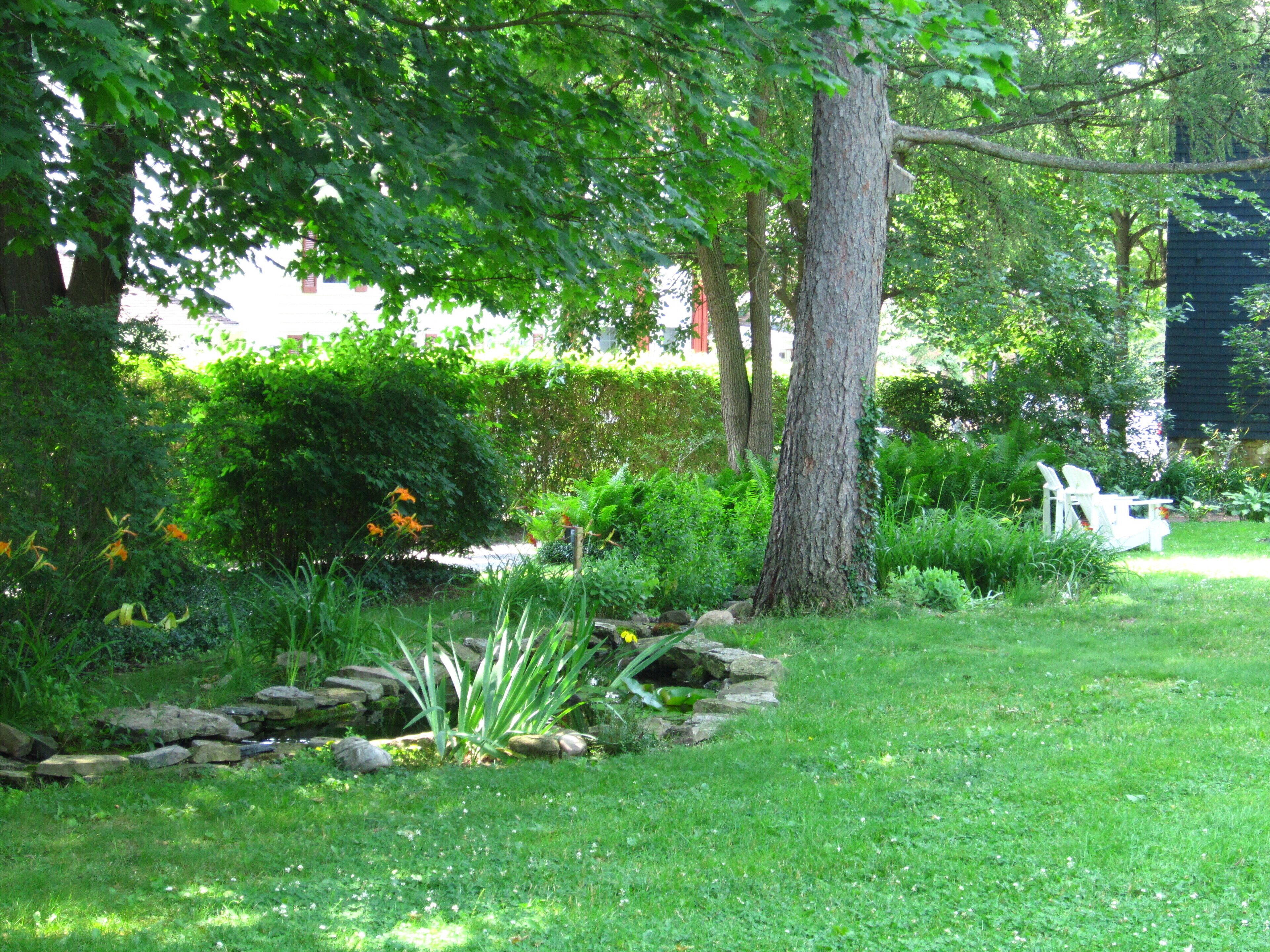 Um jardim com gramado, um pequeno jardim de pedras e uma cadeira branca.