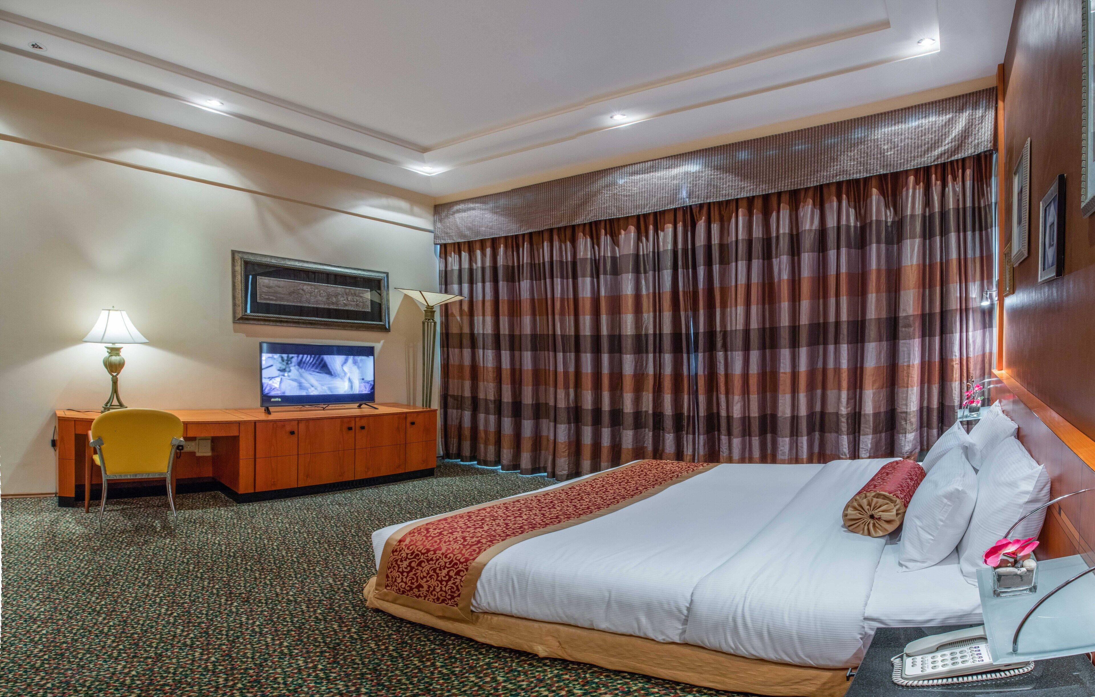 Quarto de hotel com uma cama, uma escrivaninha com cadeira, televisão e telefone.